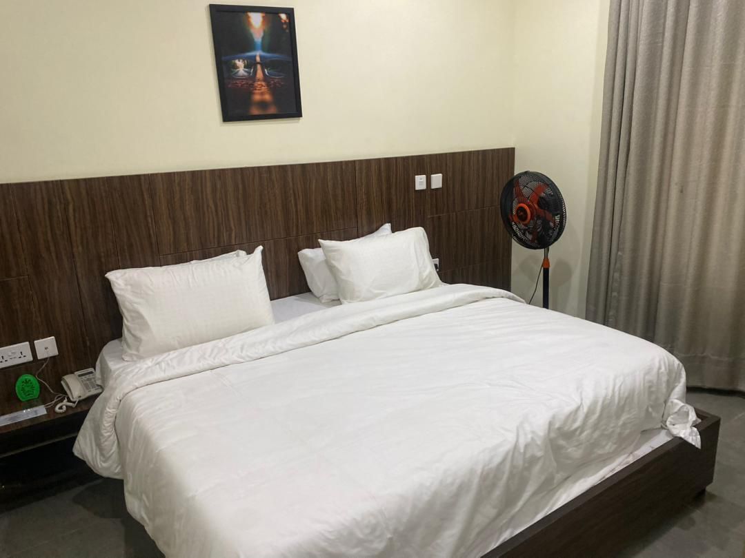 Quarto de hotel com uma cama grande, um ventilador fixado na parede e um quadro sobre a cama.
