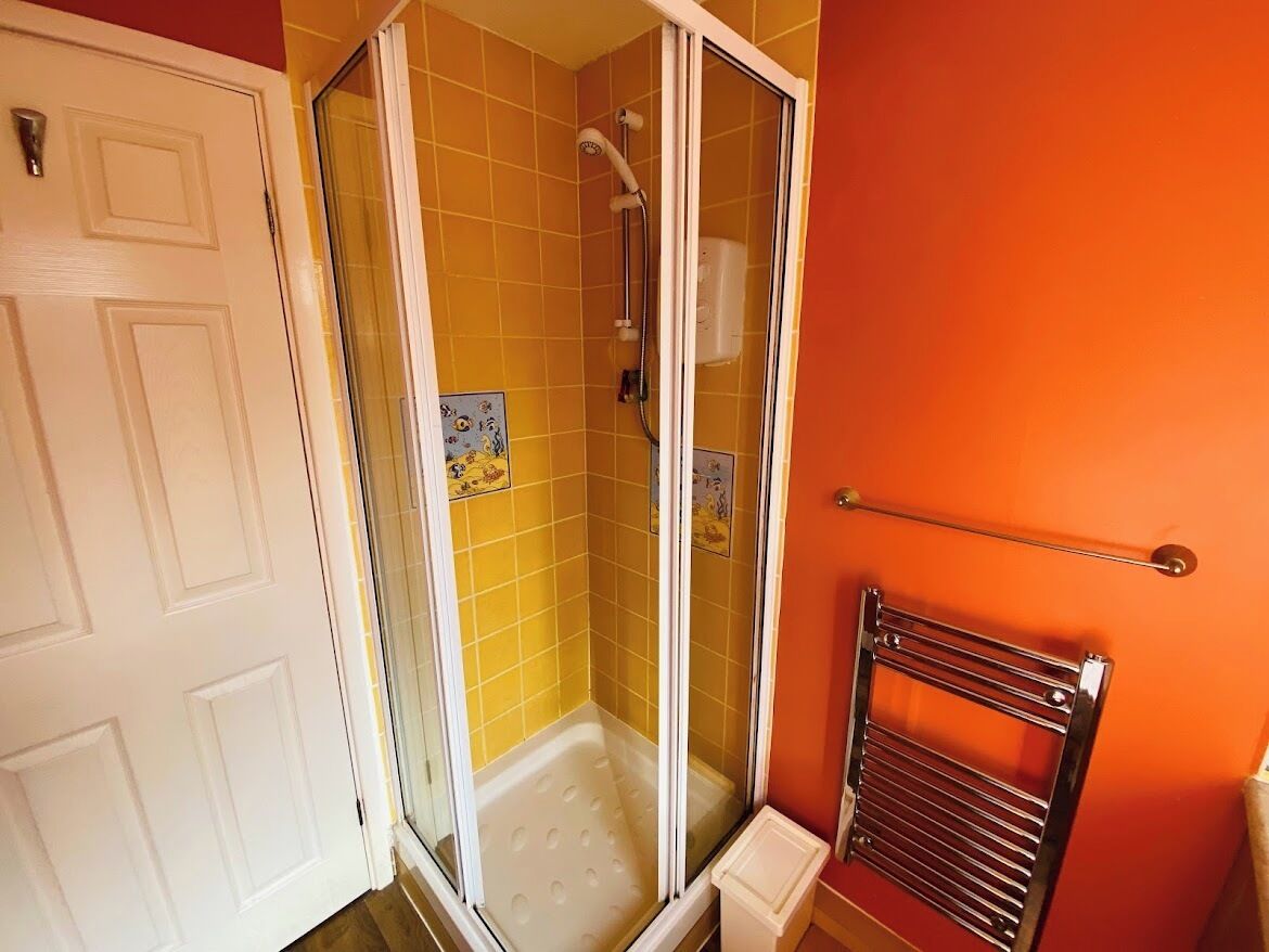 Casa de banho com chuveiro, porta branca e porta-toalhas.