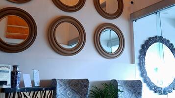 Um hall com vários espelhos fixados na parede, um balcão de recepção, assentos estampados e uma janela grande.