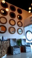 Um hall com vários espelhos fixados na parede, um balcão de recepção, assentos estampados e uma janela grande.