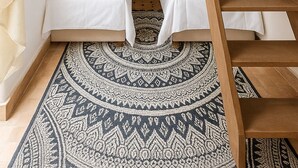 Quarto compacto com uma cama de solteiro, uma escada de madeira e um tapete estampado.