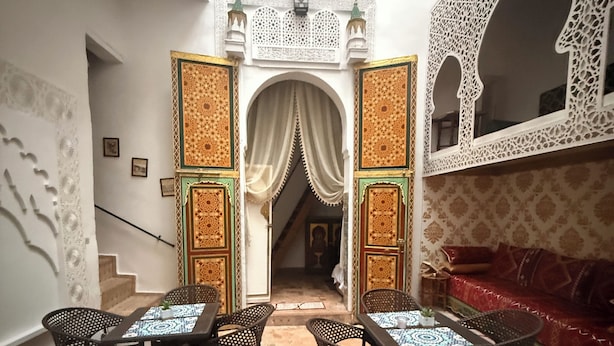 Um interior com um arco central, uma área de estar com mesas e cadeiras, e um sofá estampado.