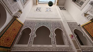 Vista interna de um edifício tradicional com delicados trabalhos em brises-soleil brancos, portas em arco e um claraboia.