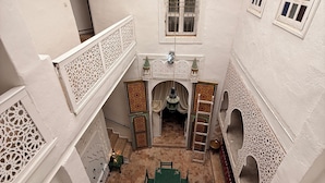 Um pátio interior com uma mesa central, arcos decorativos e um candeeiro suspenso.