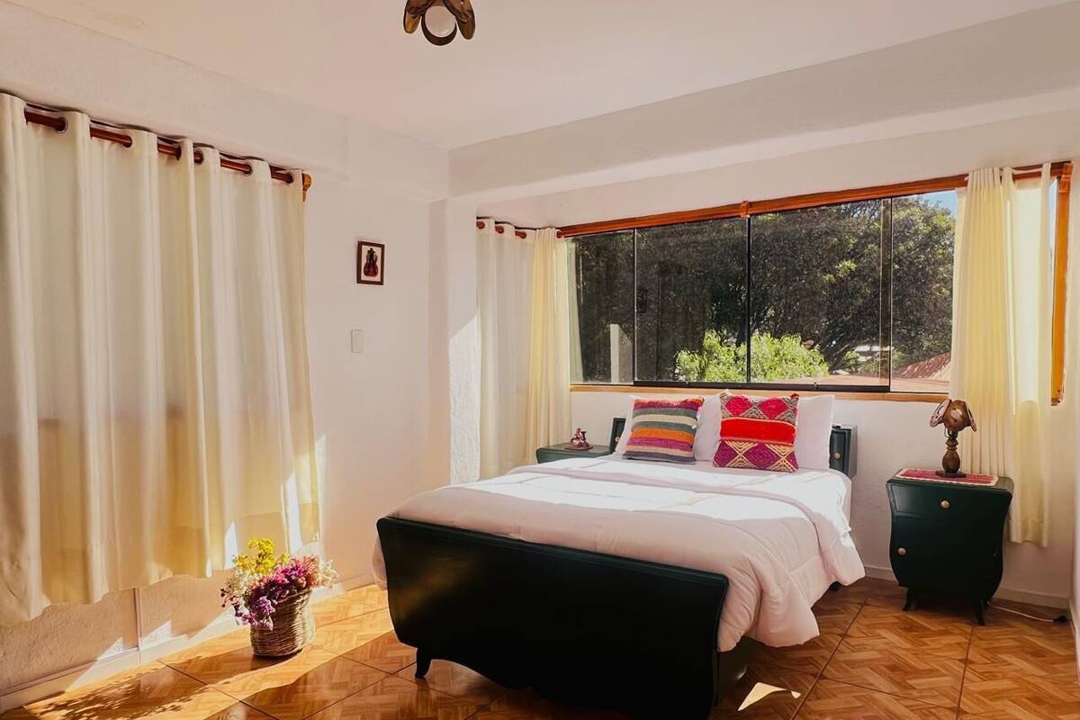 Quarto com cama, janela, mesa de cabeceira e planta em vaso.