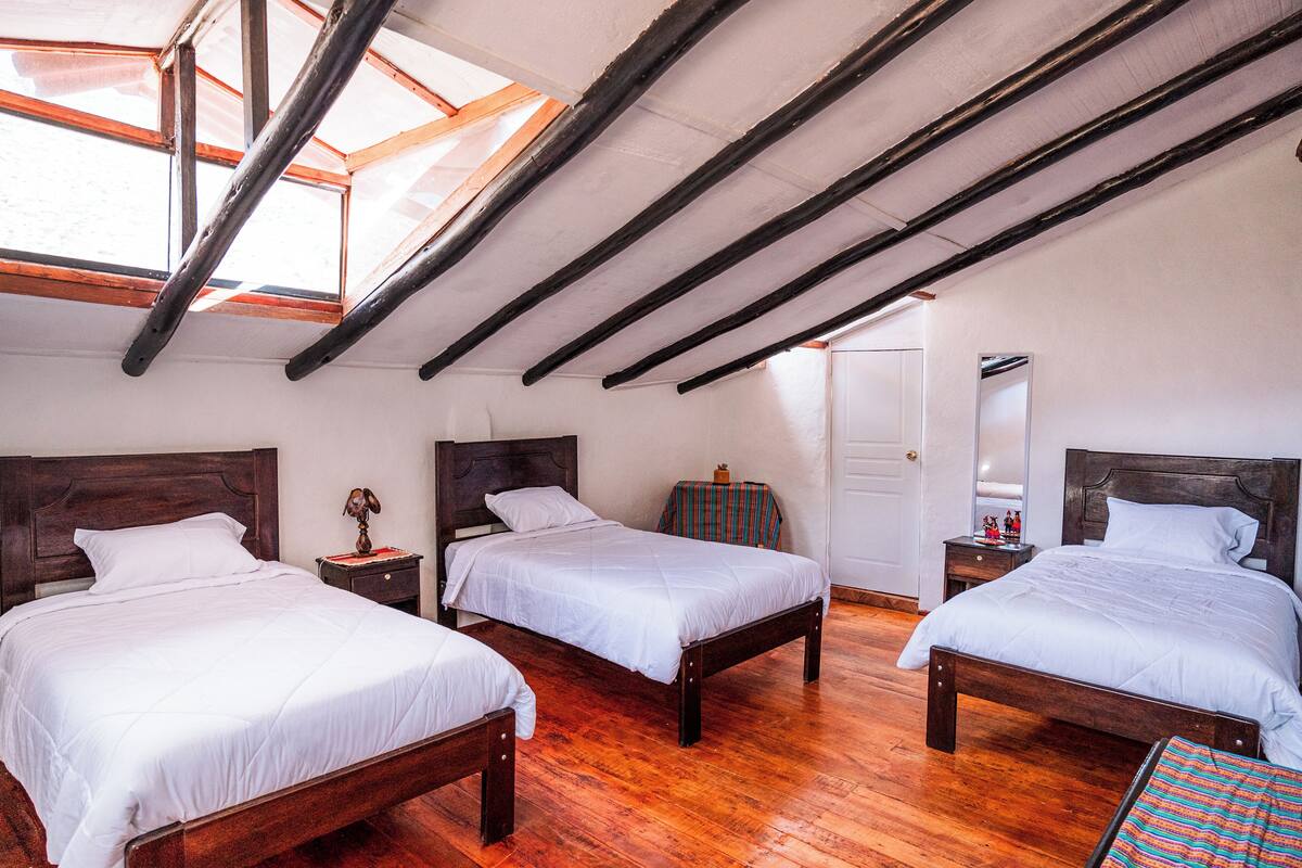 Quarto com duas camas, piso de madeira, claraboia e porta.