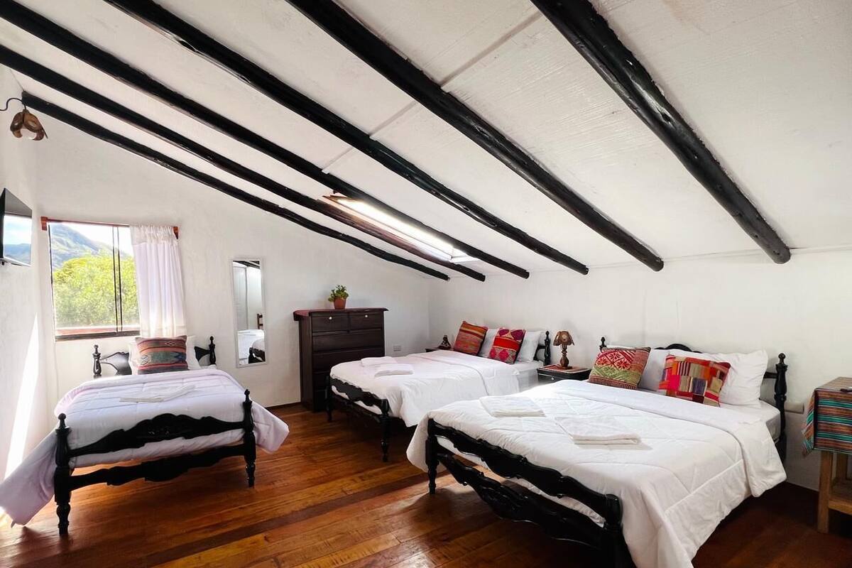 Quarto com três camas, piso de madeira e teto inclinado.