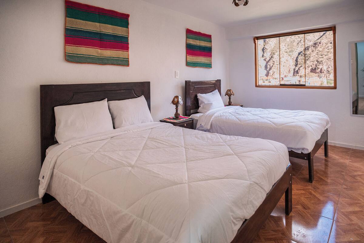 Quarto com duas camas, cabeceiras de madeira e uma janela grande com vista para árvores.