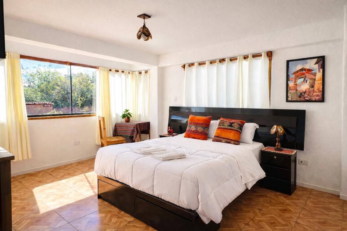 Quarto com cama, cortinas, televisão, mesa de cabeceira e quadro na parede.