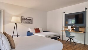 Quarto de hotel com duas camas, uma escrivaninha, televisão de tela plana, luminária e um quadro na parede.