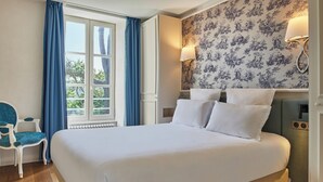 Quarto com uma cama grande, uma cadeira, janela com cortinas e papel de parede floral.