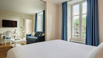 Quarto de hotel com uma cama grande, uma escrivaninha com cadeira, um sofá, uma televisão e uma janela com cortinas.