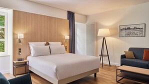 Quarto de hotel moderno com uma cama grande, uma escrivaninha, uma cadeira, um sofá e um abajur.