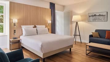 Quarto de hotel moderno com uma cama grande, uma escrivaninha, uma cadeira, um sofá e um abajur.