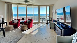 Varanda ampla vista para o mar, com cadeiras vermelhas, uma mesa e um ventilador de teto.