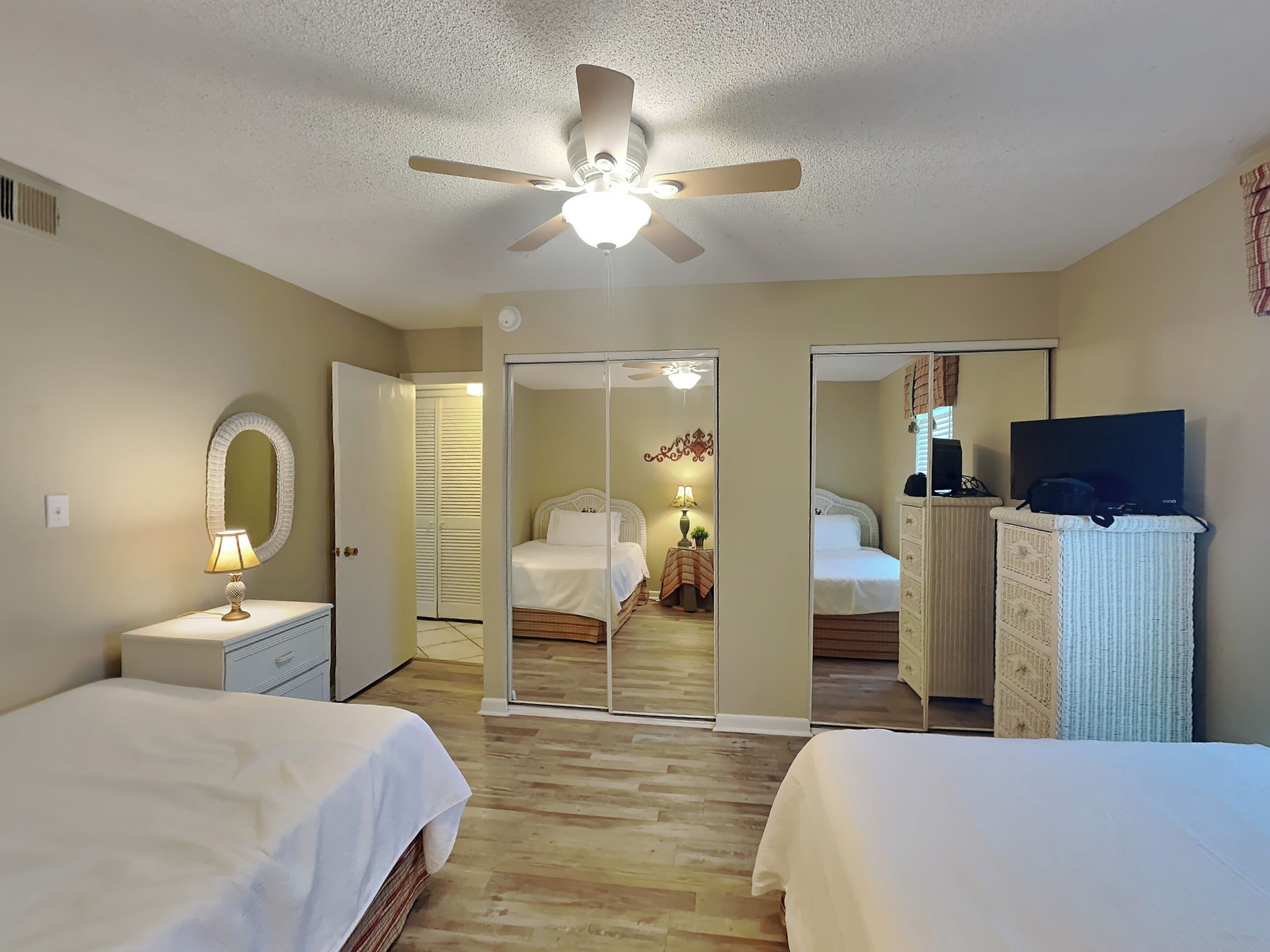 Quarto de hotel com duas camas, um ventilador de teto, uma televisão e um espelho.
