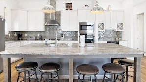 Cozinha moderna com uma ilha grande, eletrodomésticos de aço inoxidável e iluminação pendente.