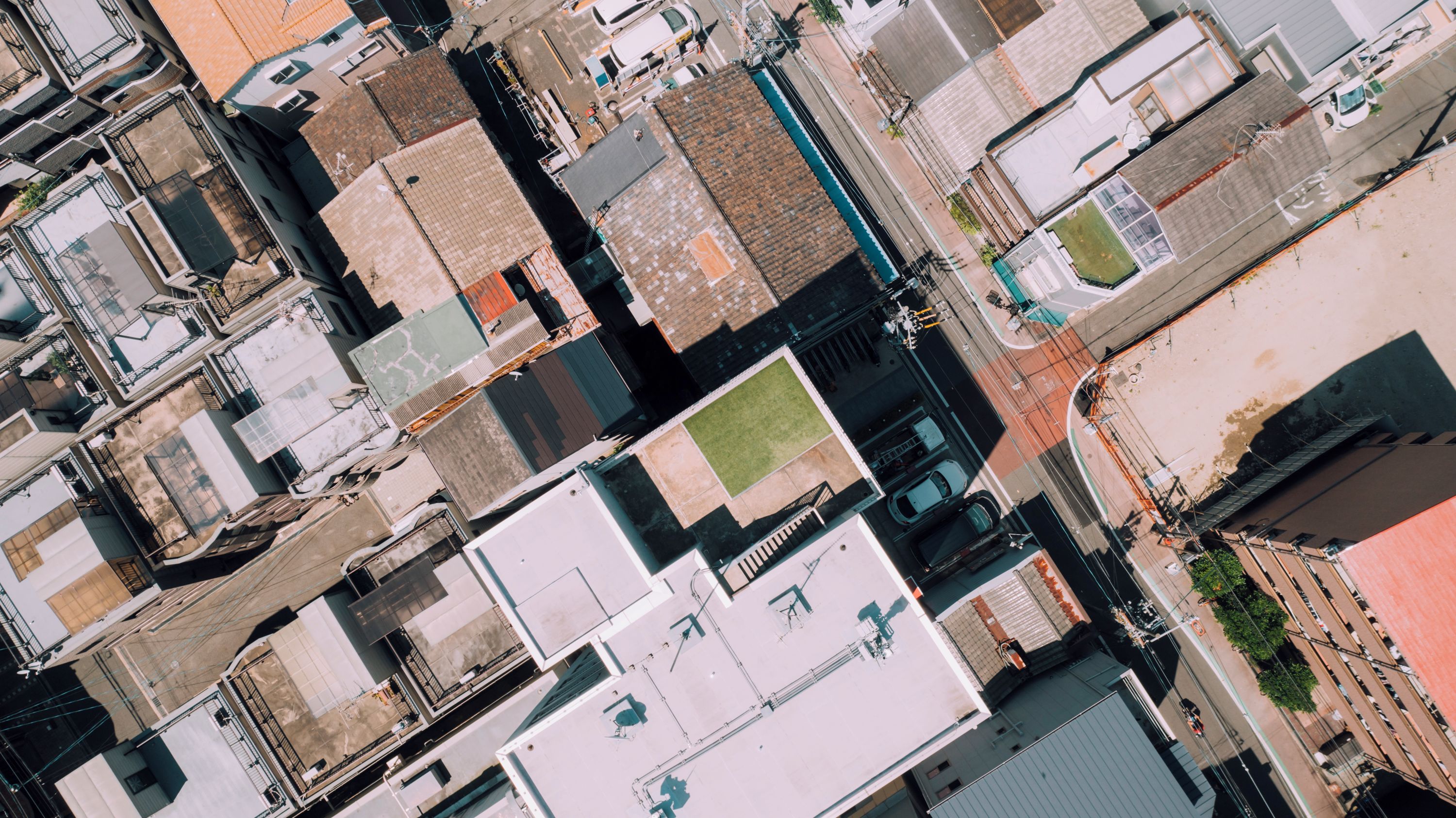 Vista aérea de uma área urbana densamente povoada com diversos edifícios, incluindo um grande edifício branco com telhado plano e um edifício menor com telhado inclinado.