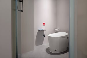 Um banheiro moderno com vaso sanitário, uma prateleira pequena e um botão de emergência vermelho na parede.