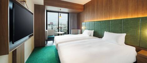 Quarto de hotel com duas camas, televisão, varanda com vista e tapete verde.