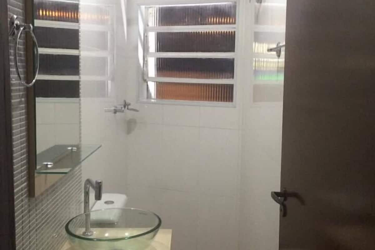 Uma casa de banho moderna com uma sanita, lavatório de vidro, espelho e janela com persianas.
