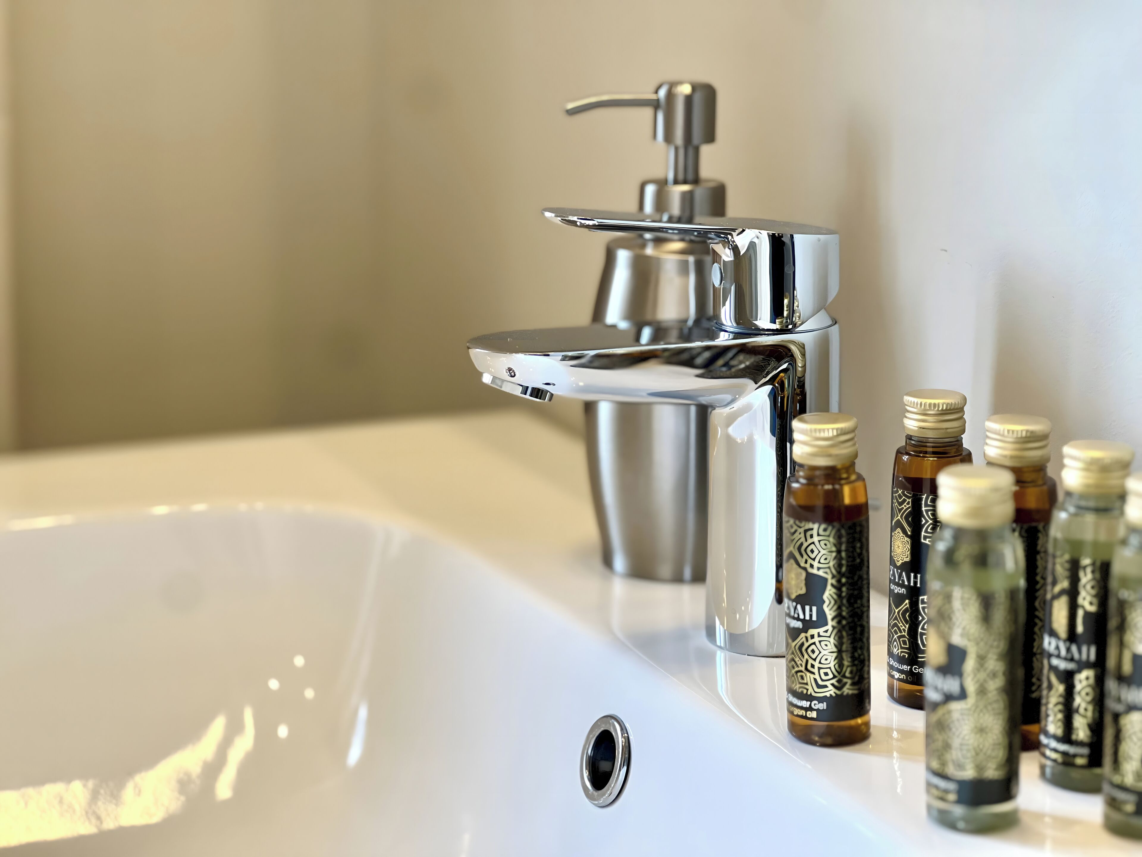 Uma pia de banheiro com torneira cromada e vários pequenos frascos de produtos para cabelo.