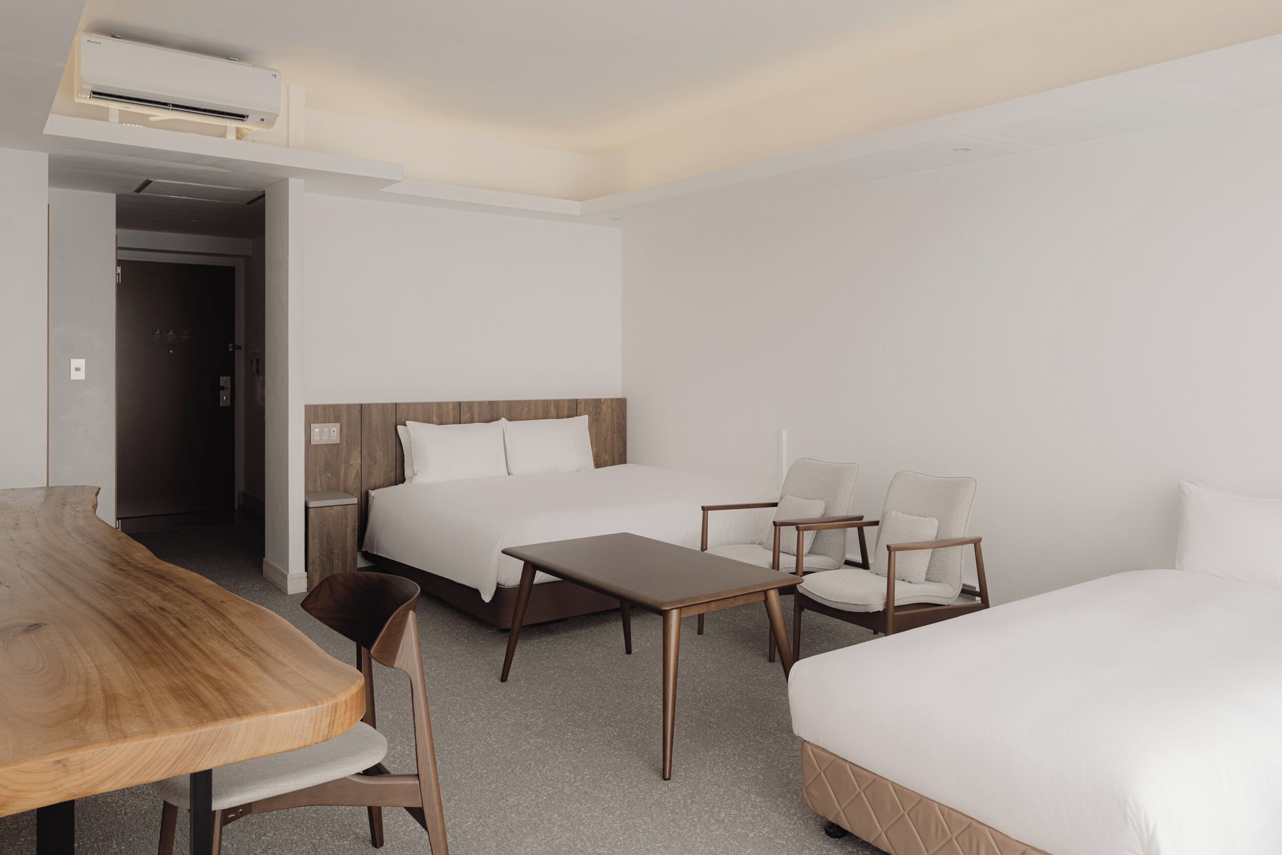 Quarto de hotel com duas camas, uma mesa de madeira e duas cadeiras.