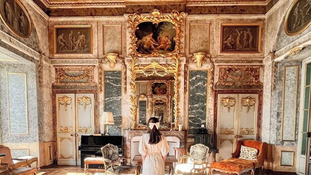 Quarto luxuoso com detalhes dourados elaborados, um piano de cauda e obras de arte clássicas.