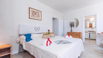 Quarto de hotel com cama, mesa de cabeceira, espelho, pequena mesa com um vaso de flores e porta que dá para um banheiro.