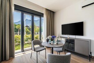 Quarto moderno com uma janela ampla, televisão de tela plana e uma mesa de jantar redonda com cadeiras.