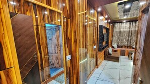 Um interior moderno com painéis de madeira, divisória de vidro, área de estar com sofá e almofadas, e televisão fixada na parede.