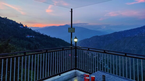 Uma varanda com vista para uma paisagem montanhosa ao entardecer.