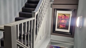Uma escadaria com um quadro emoldurado retratando uma mão segurando um rosto, e uma placa com a inscrição 'RESTING BITCH FACE'.