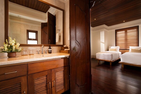 Quarto de hotel com toucador de madeira, um espelho grande, cama com roupa branca e vista para o exterior através de uma janela.