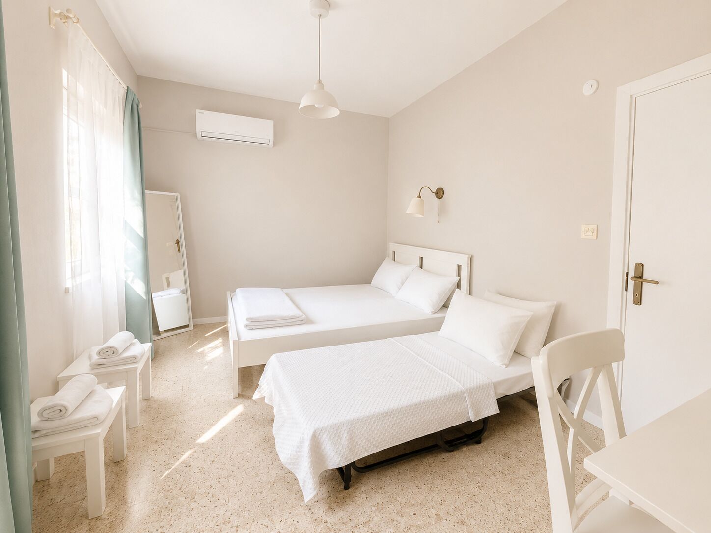 Quarto minimalista com duas camas, uma escrivaninha, uma cadeira e um banheiro com espelho.