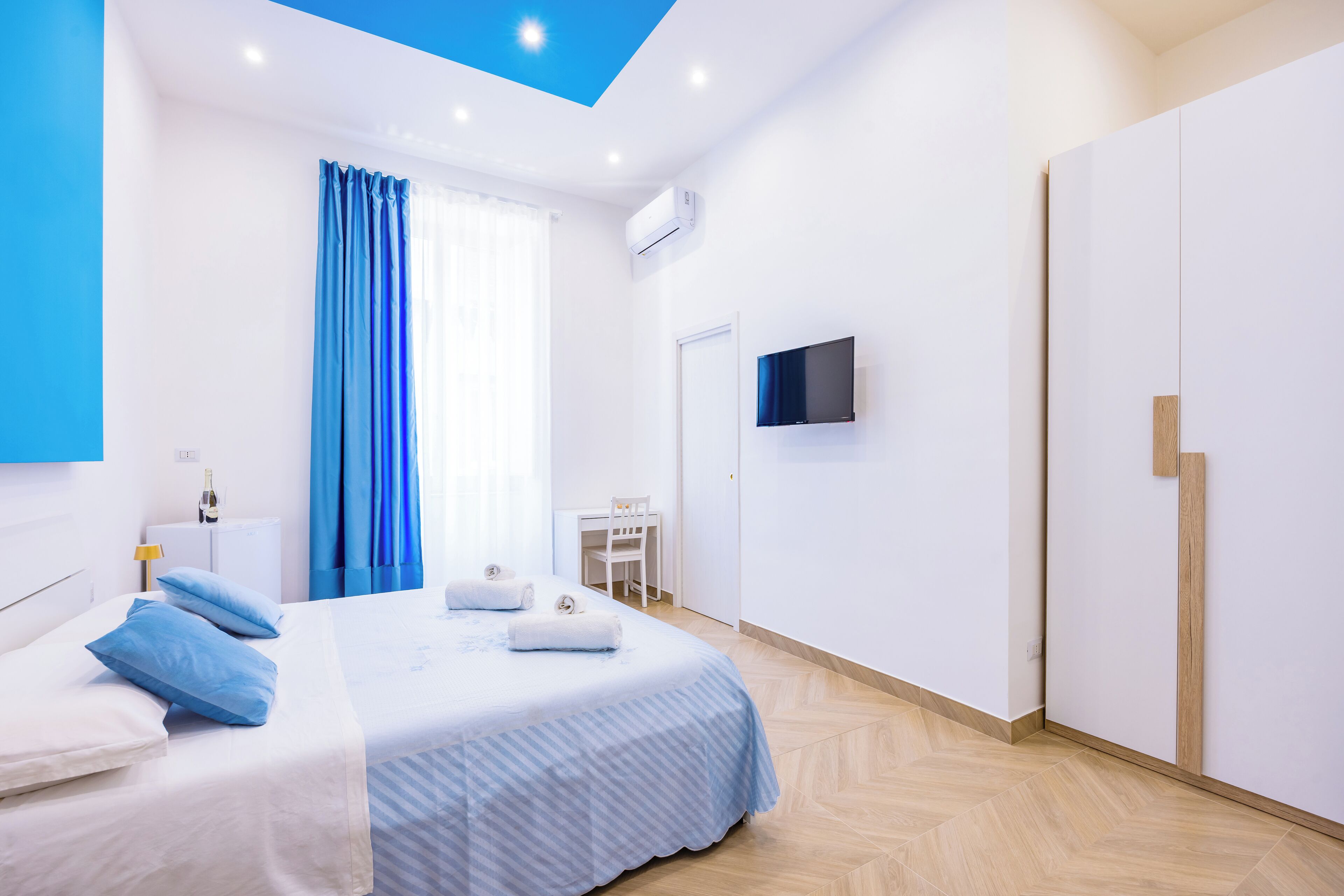 Quarto de hotel moderno com cama, escrivaninha, cadeira, televisão e ar condicionado.