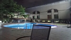 Piscina com uma cadeira em primeiro plano, cercada por um edifício com várias janelas e chão de azulejos.