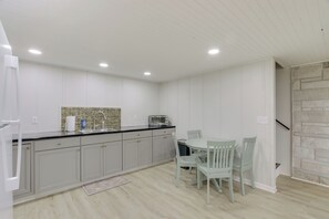 Uma cozinha moderna com armários brancos, bancada de granito, torradeira embutida e um espaço de jantar com mesa redonda e cadeiras.