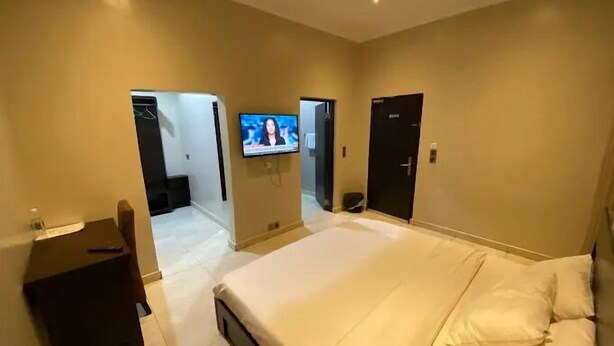 Quarto de hotel com uma cama grande, uma escrivaninha e uma TV na parede.