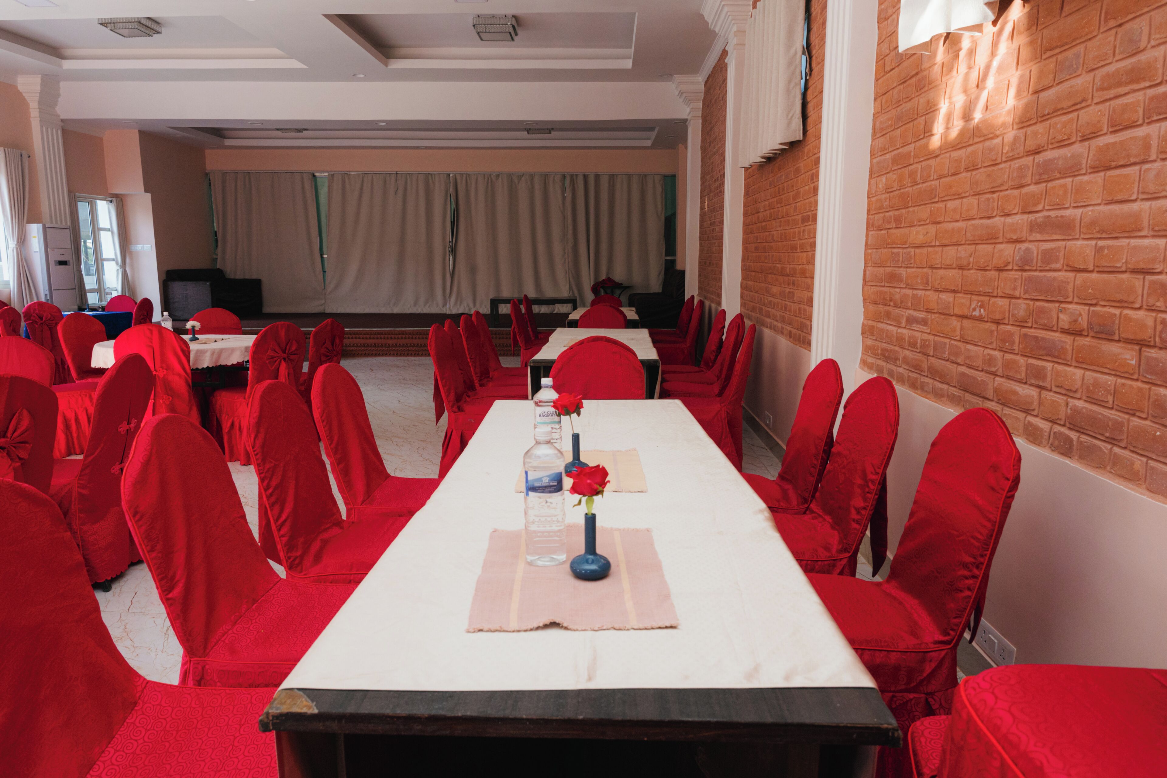 Uma sala de conferências com cadeiras vermelhas, uma mesa comprida e uma parede de tijolos.