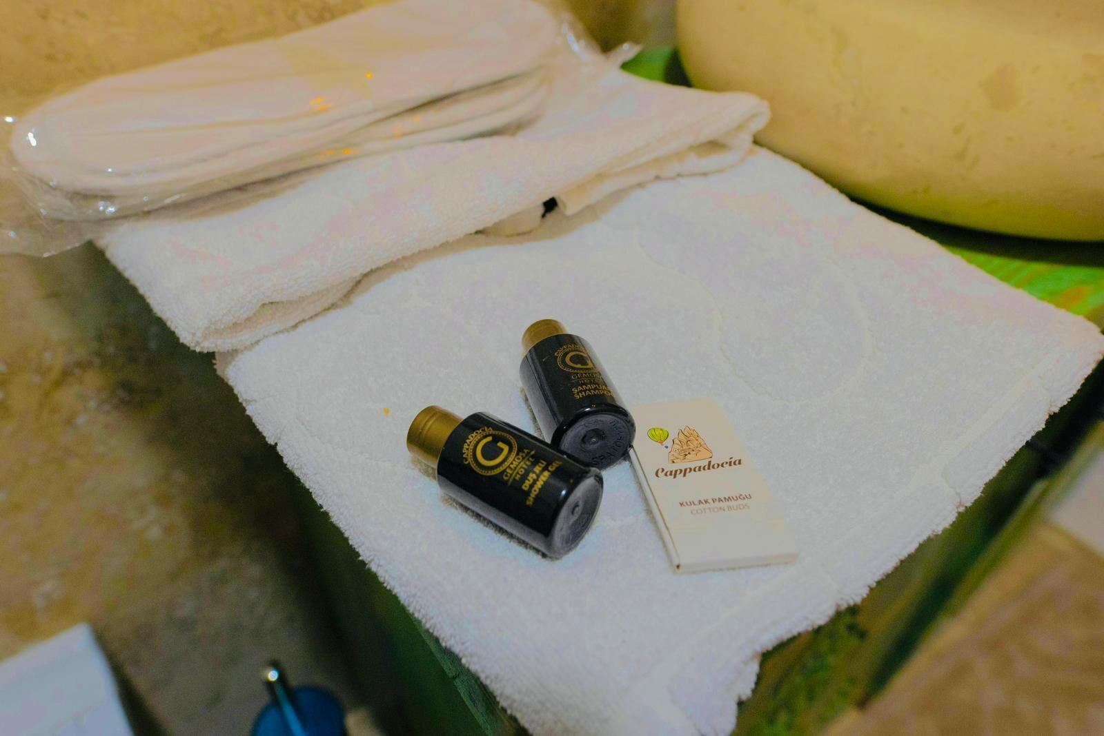 Casa de banho com toalha branca, dois frascos de champô e um cartão com a inscrição 'Capadócia'.