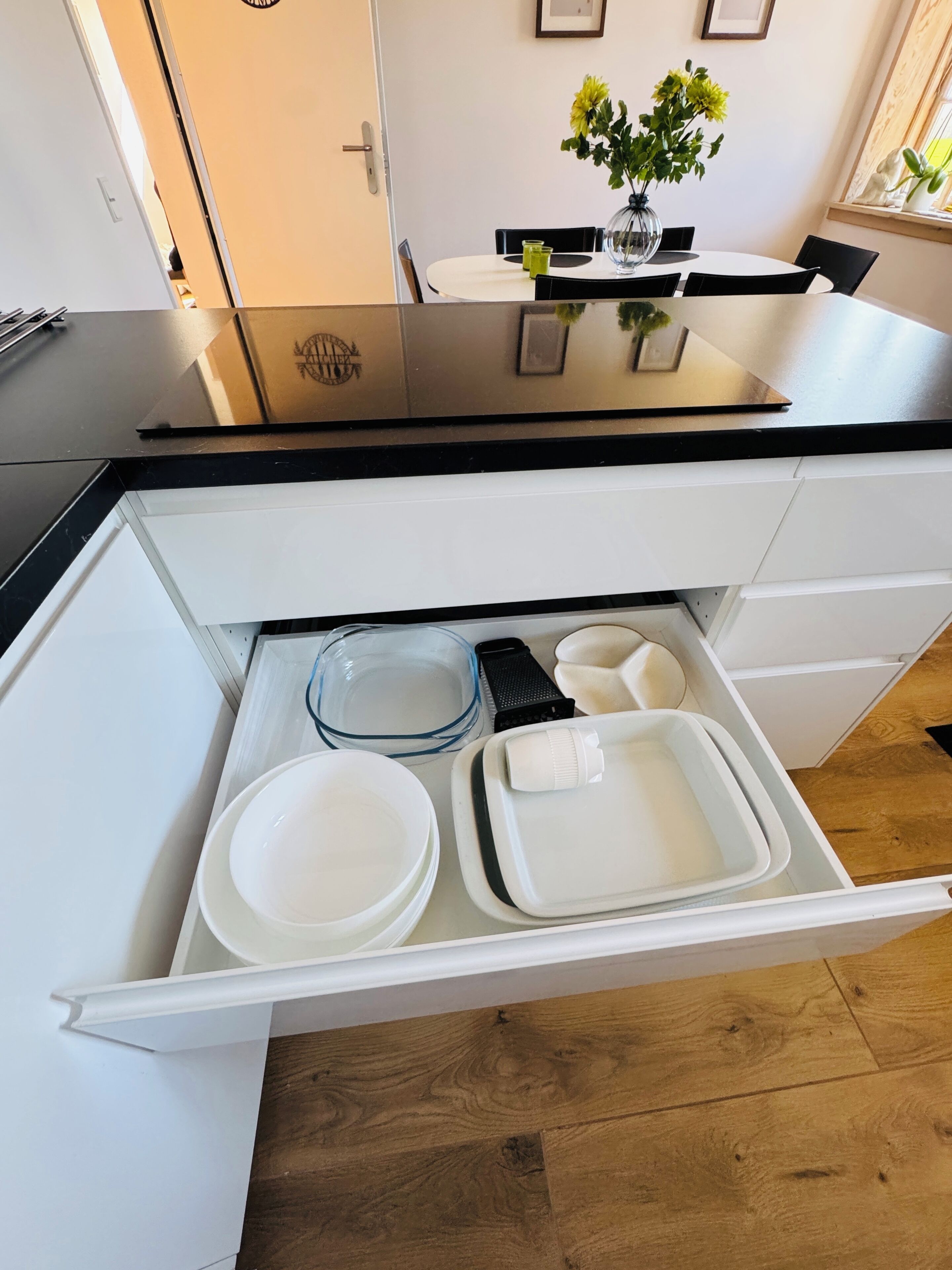 Uma cozinha com bancada preta, armários brancos e piso de madeira.
