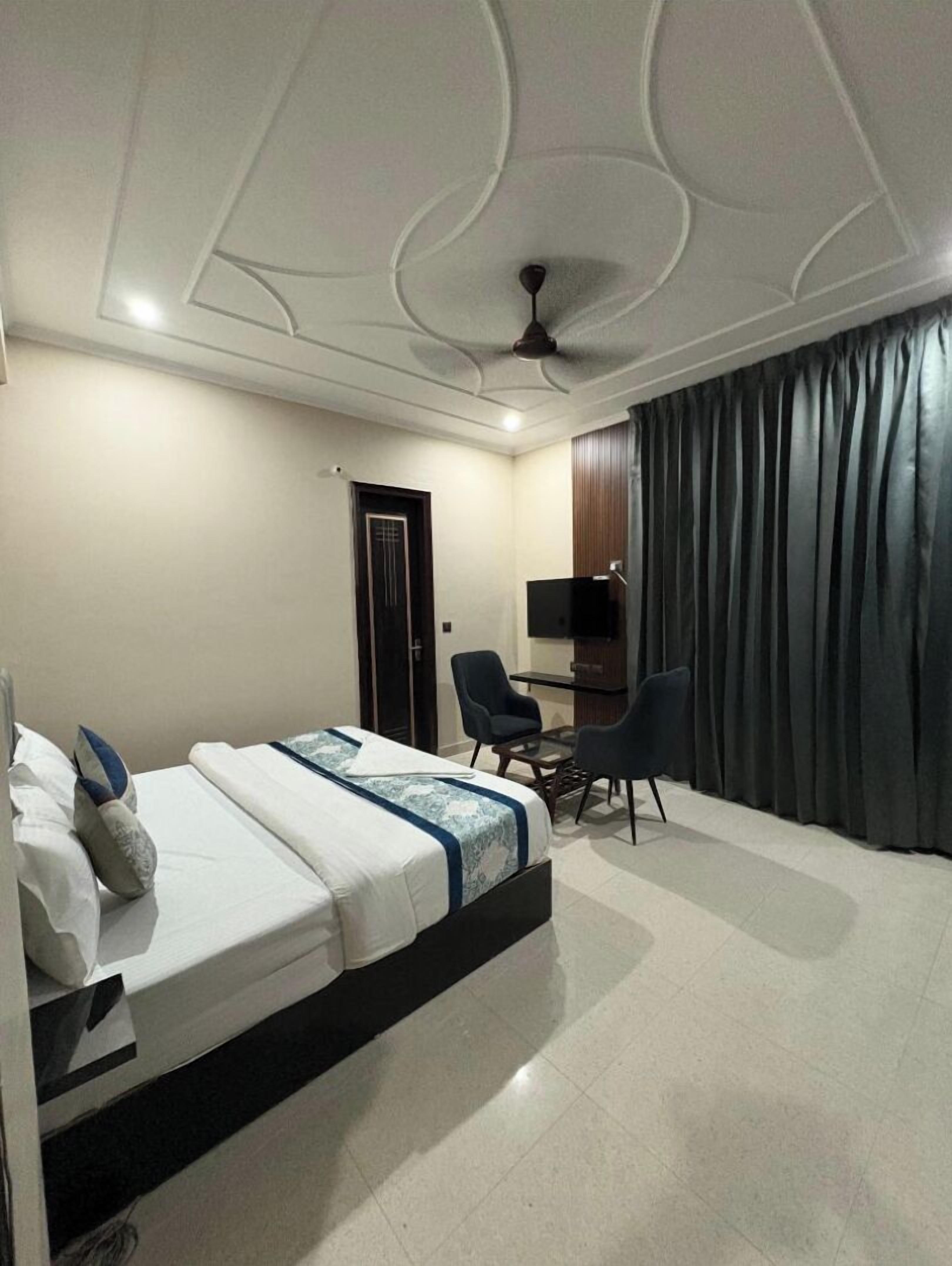 Quarto de hotel com cama, escrivaninha, cadeira, televisão e cortina.