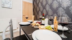 Uma área de refeições com mesa posta para dois, incluindo pratos, copos, queijo, uvas e palitos de pão.
