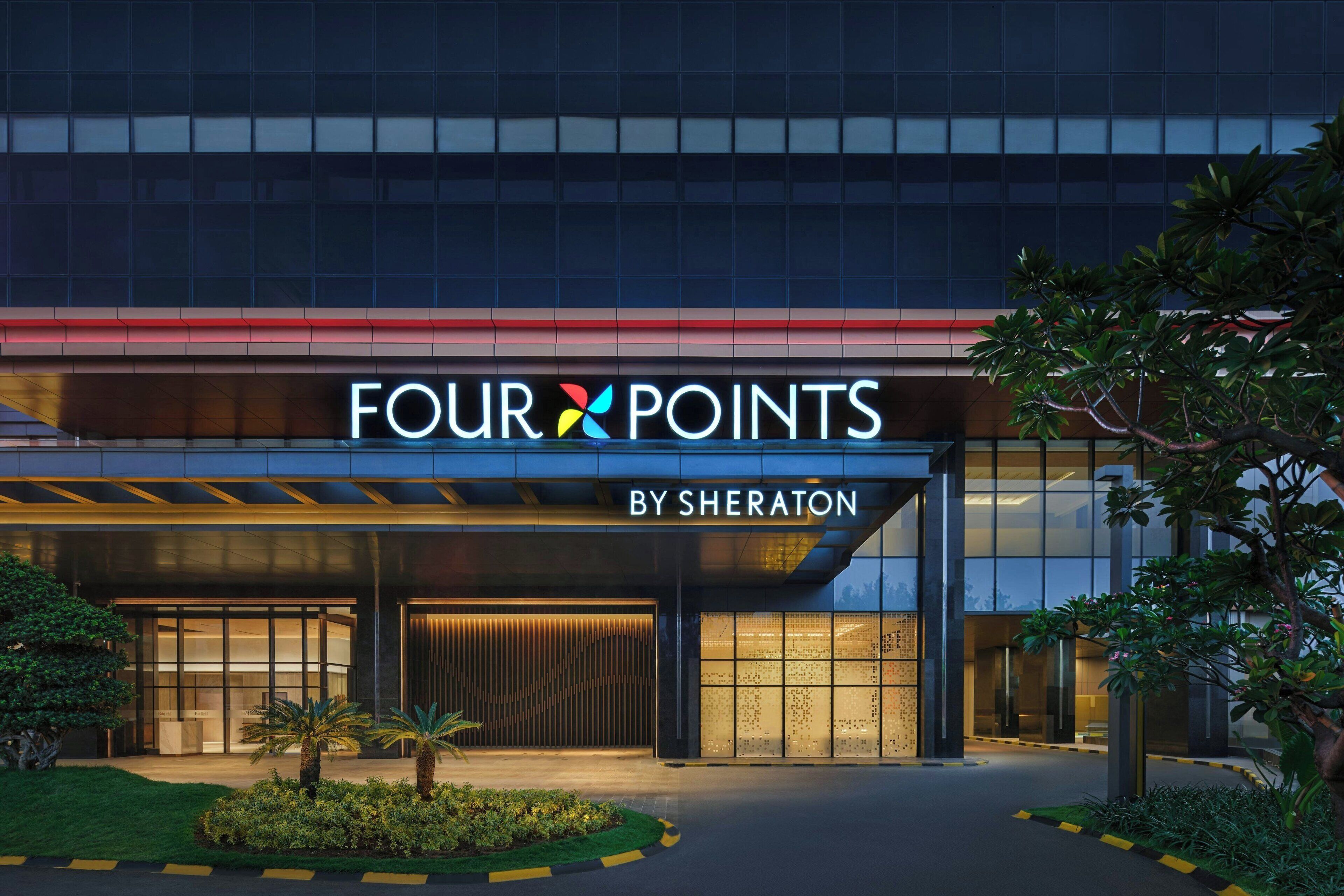 Entrada moderna de hotel com fachada de vidro e placa com a inscrição "FOUR POINTS BY SHERATON".