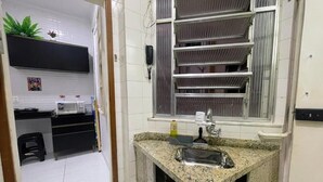 Uma cozinha compacta com bancada de granito, pia embutida e janela com persianas.