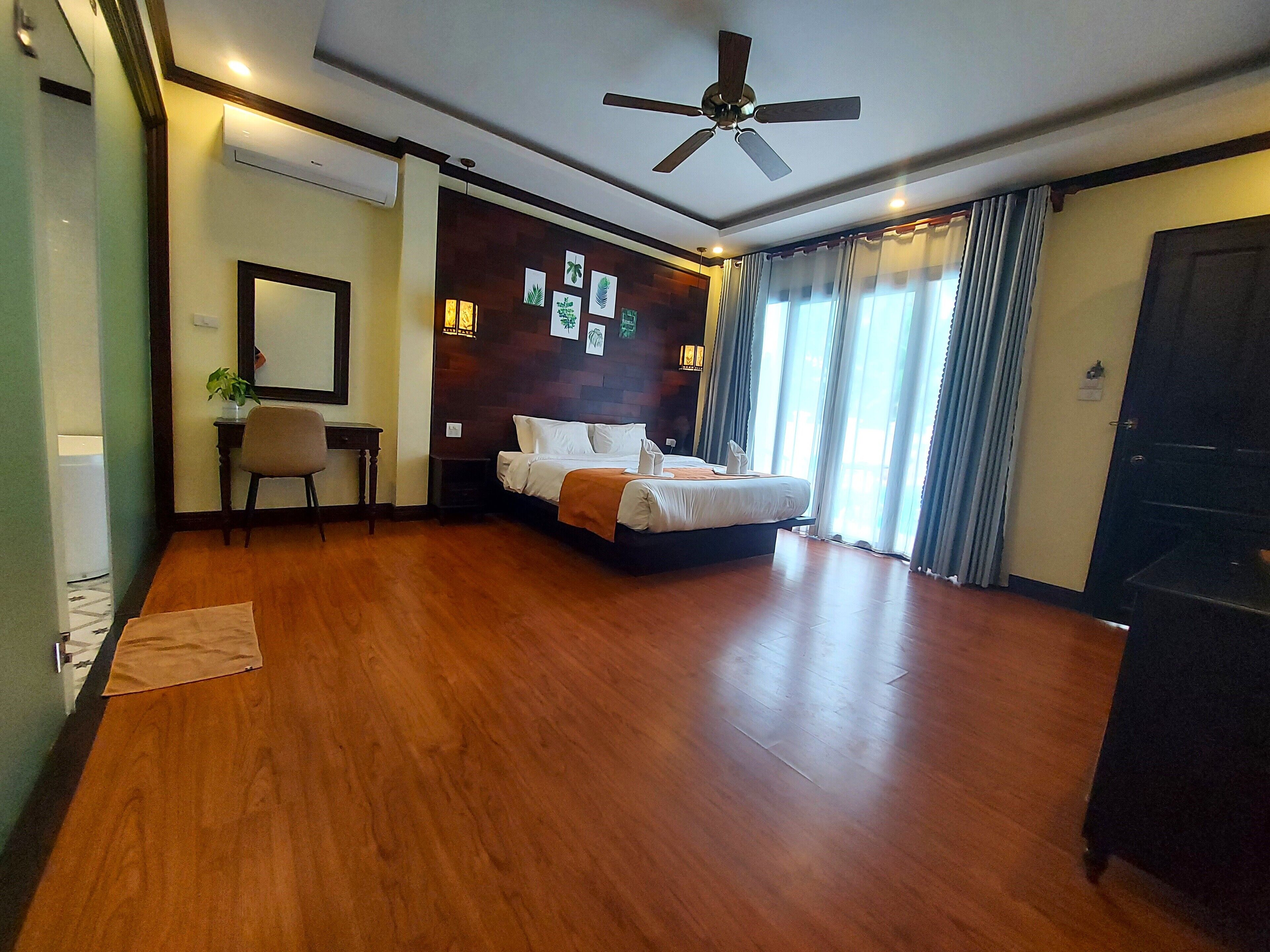 Um quarto de hotel espaçoso com uma cama grande, uma escrivaninha e um ventilador de teto.