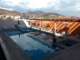 Piscina no terraço com várias áreas, rodeada por espaços de estar ao ar livre com guarda-sóis.
