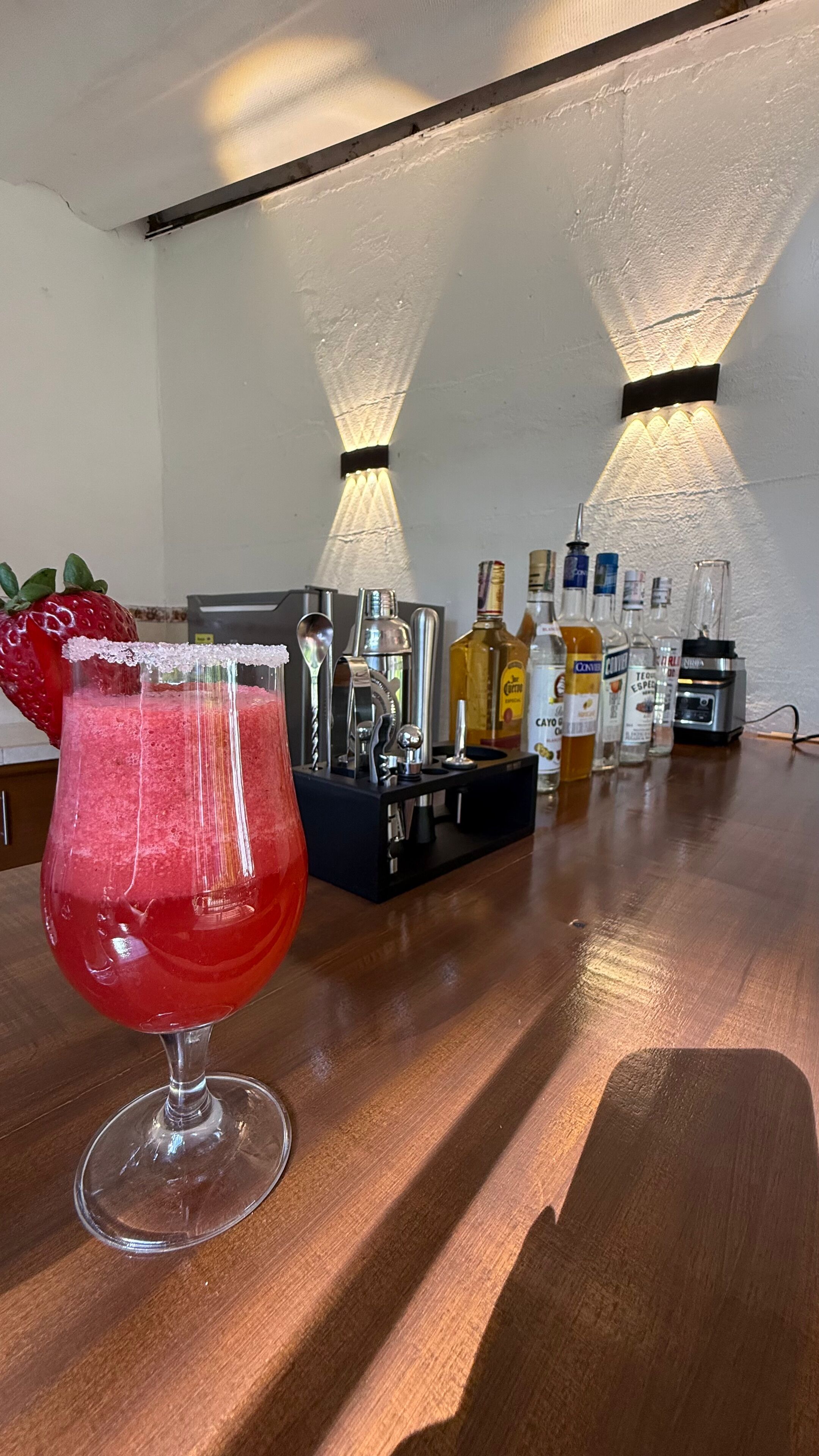 Uma área de bar com um coquetel num copo, vários frascos e utensílios de bar.