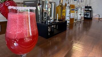 Uma área de bar com um coquetel num copo, vários frascos e utensílios de bar.